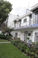 Um edifício de dois andares com uma varanda, uma porta com o número 106, e um jardim com diversas plantas e flores.