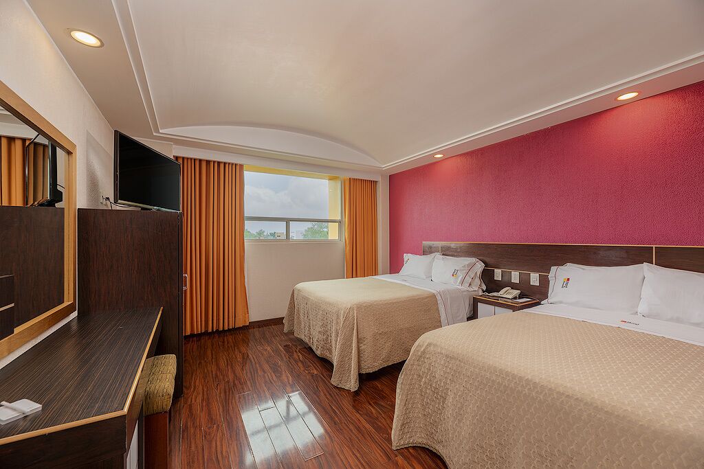 Quarto de hotel com duas camas, uma escrivaninha, uma TV e uma janela com cortinas.