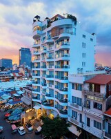 Um hotel com vários andares, varandas, um jardim no terraço e vista para a paisagem urbana ao redor.