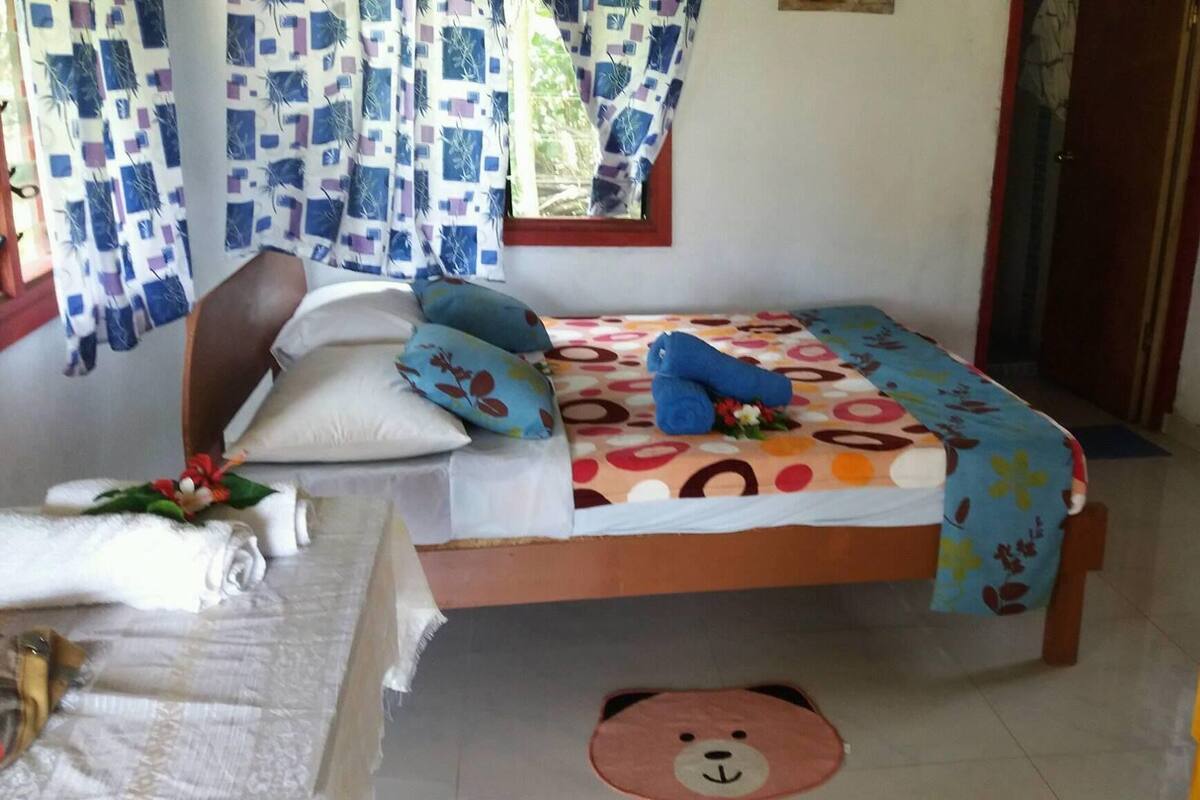 Quarto com cama, almofadas, mesa de cabeceira, cadeira e um tapete em formato de urso no chão.
