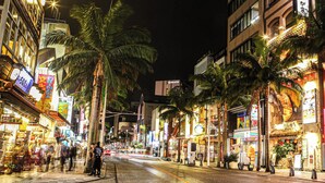 Cena noturna de rua com palmeiras, placas iluminadas e prédios.