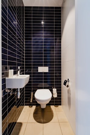 Um banheiro moderno com parede revestida de azulejos pretos, pia branca e vaso sanitário.