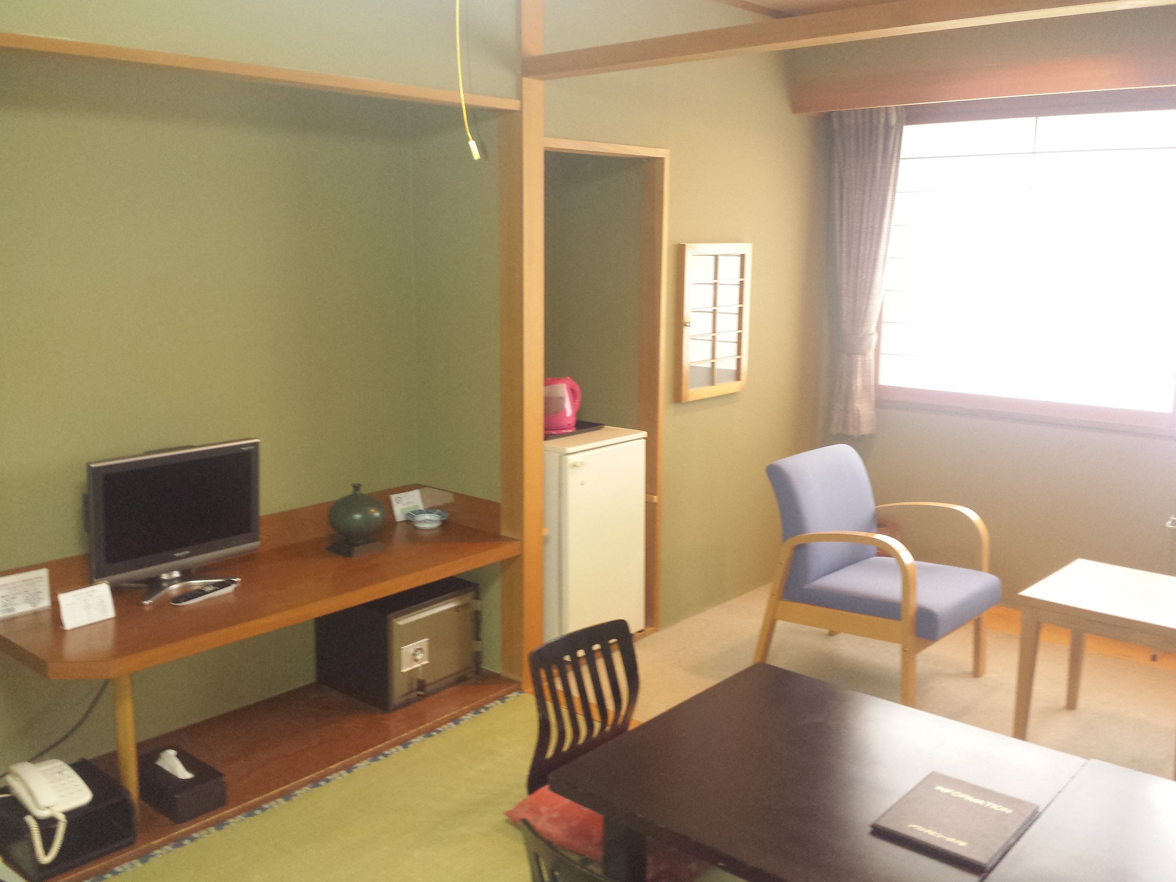 Um quarto pequeno e aconchegante com uma escrivaninha de madeira, uma cadeira, uma televisão e um frigorífico.
