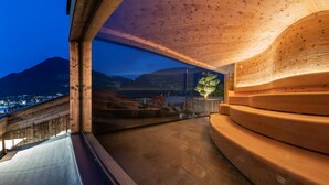 Interior moderno com um banco de madeira curvo, uma janela ampla com vista para uma paisagem montanhosa e teto de madeira.