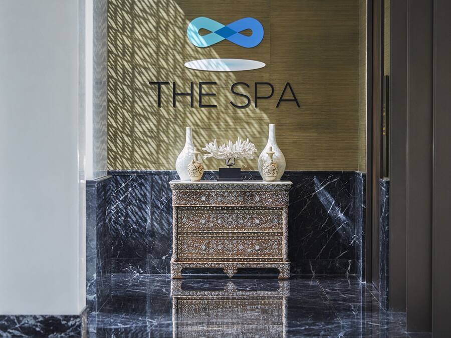Uma área de recepção com balcão de mármore, dois vasos e um painel com a inscrição 'THE SPA'.