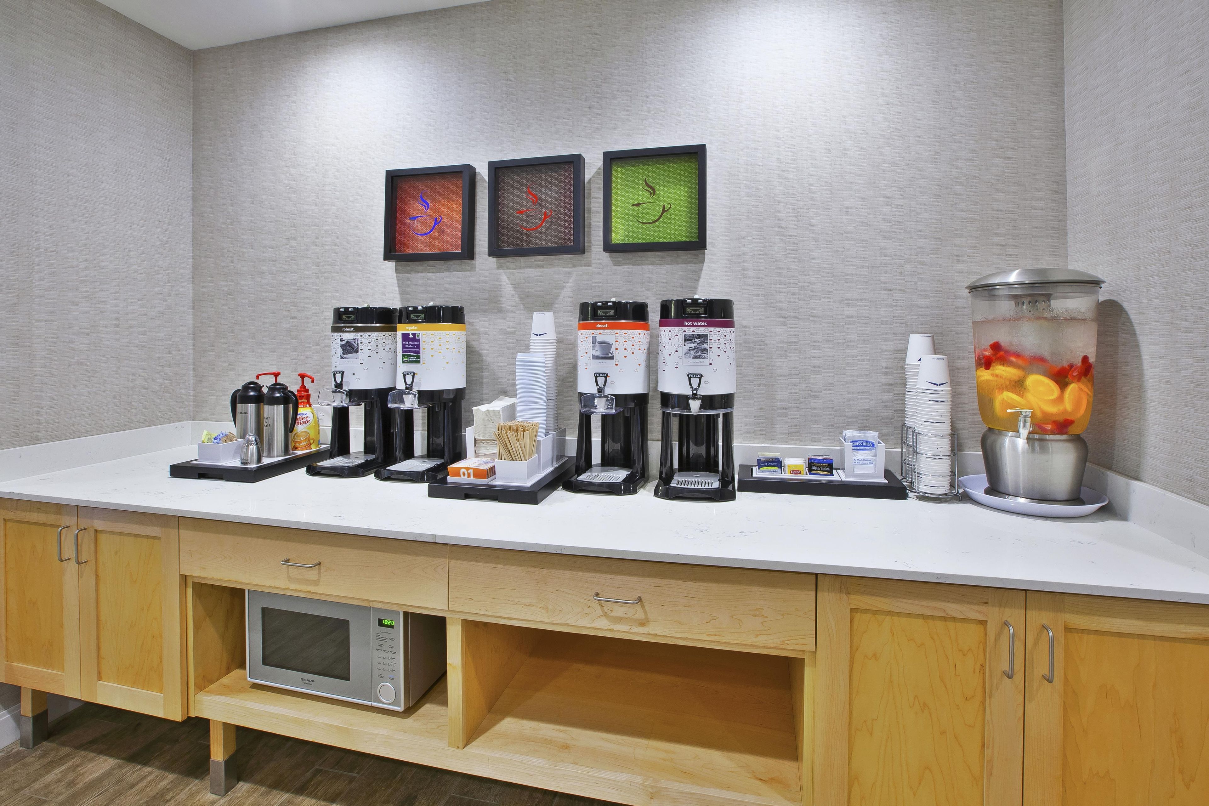 Uma estação de bebidas com serviço próprio, com várias máquinas de café, um micro-ondas e um dispensador de ponche de frutas.