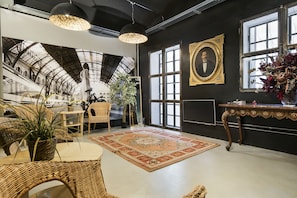 Um quarto amplo com uma janela grande, área de refeições com mobiliário de vime e um tapete decorativo.