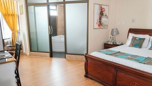 Quarto de hotel com cama de madeira, uma escrivaninha com cadeira, banheiro com banheira e porta de vidro deslizante.