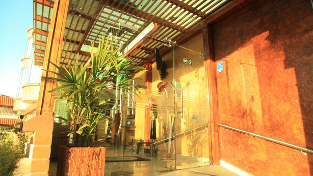 Entrada de hotel com porta de vidro, guarda-corpo de metal e um vaso de planta grande.