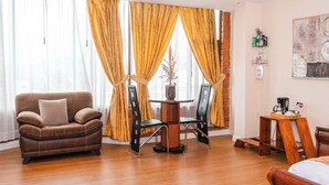 Um quarto com um sofá de couro marrom, uma mesa de jantar com cadeiras, uma cama e uma janela grande com cortinas.