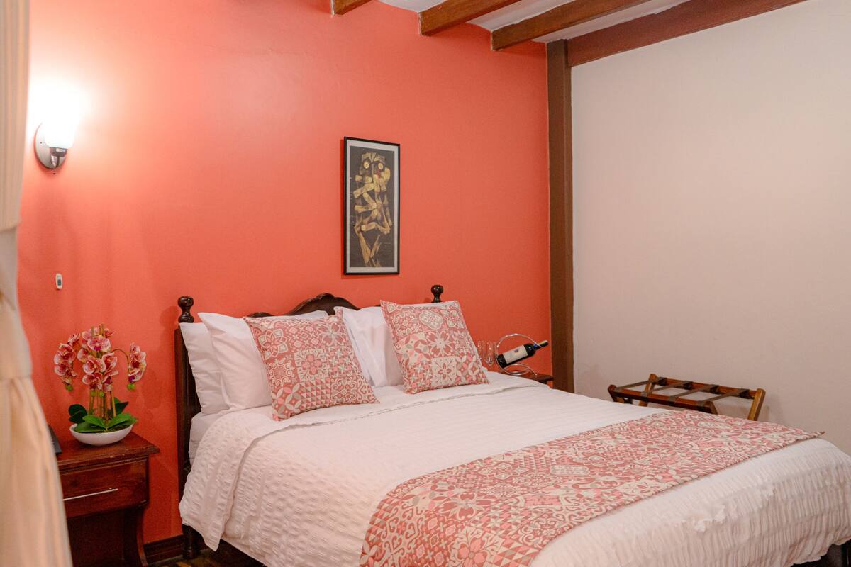 Quarto com cama, mesa de cabeceira, abajur e um quadro na parede.
