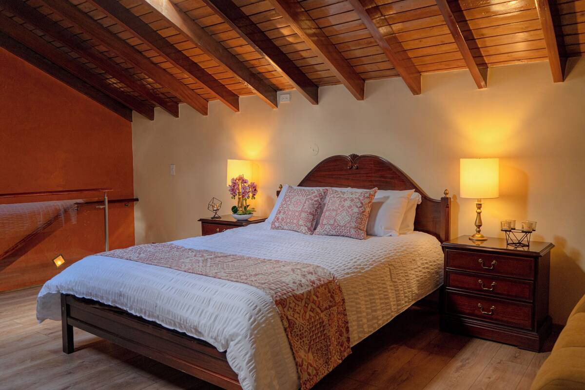 Quarto com uma cama de madeira, duas mesas de cabeceira e uma mesinha de apoio.