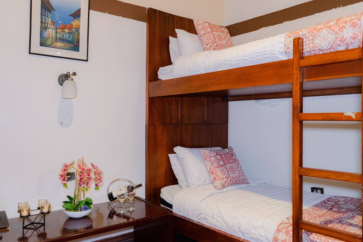 Quarto com beliche, cabeceira de madeira, quadro na parede, mesa de cabeceira com abajur e um vaso com flores.