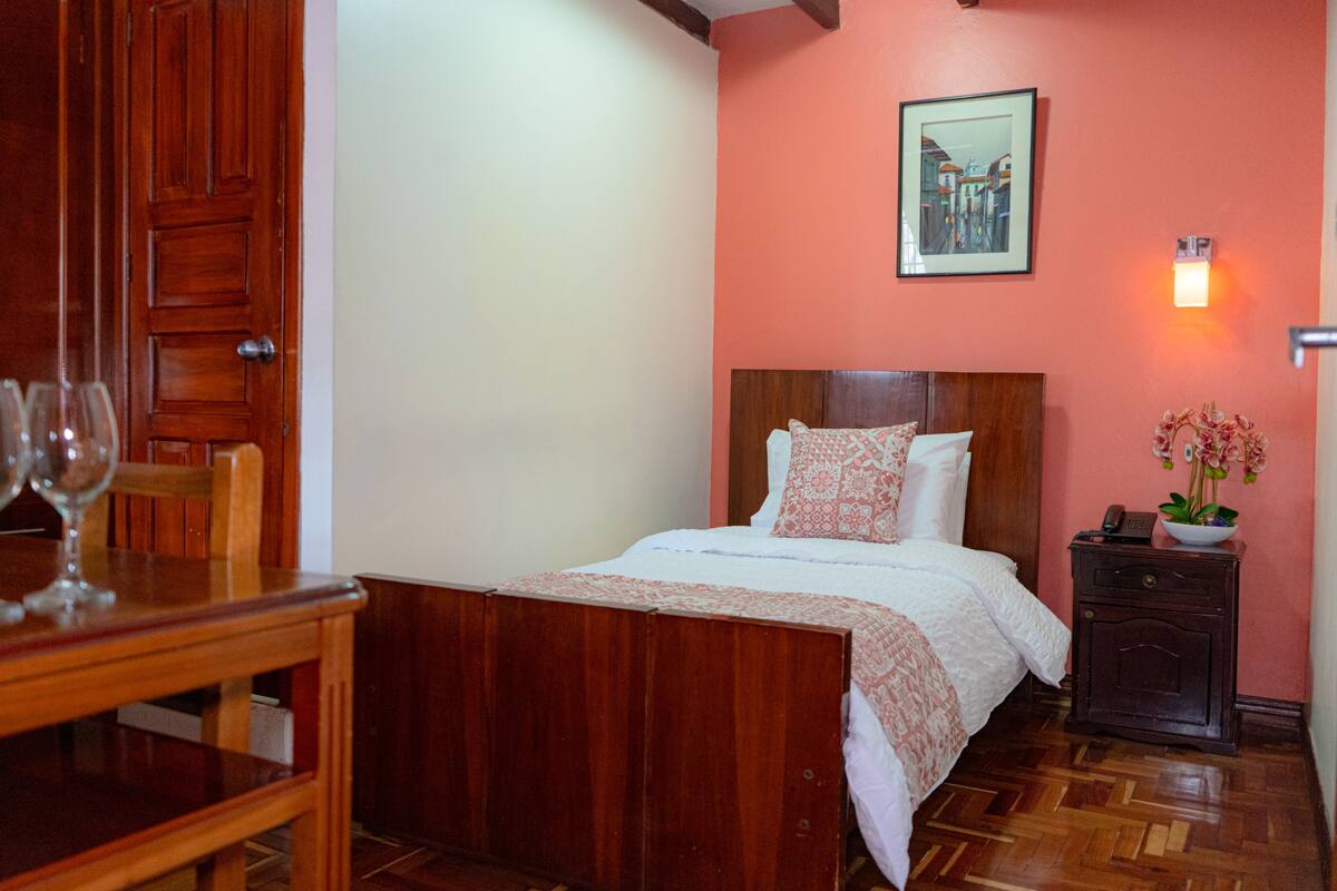 Um quarto com cama de madeira, mesa de cabeceira com abajur e mesa de jantar com cadeiras.