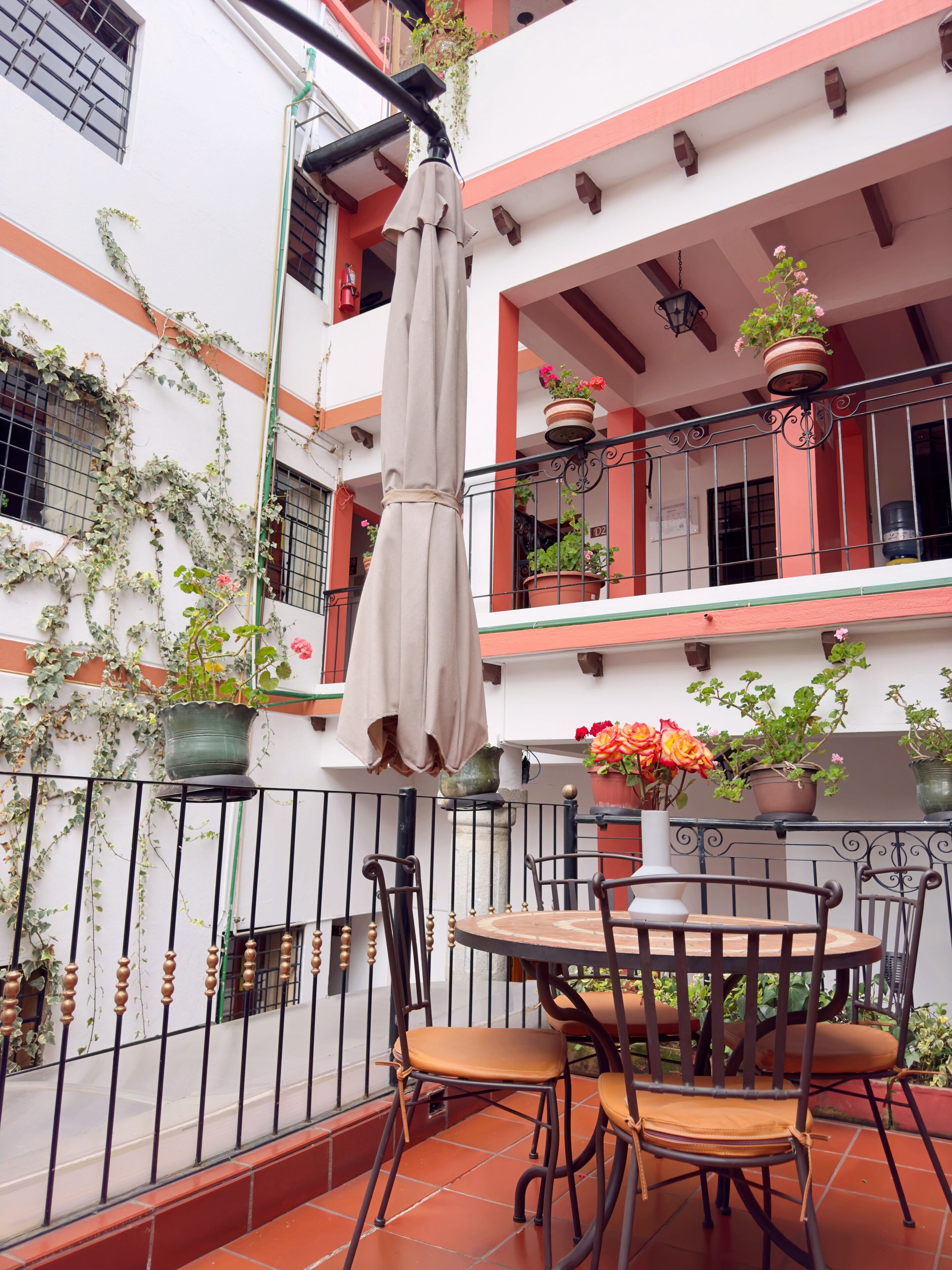 Terraço com mesa e cadeiras, rodeado por plantas em vasos e guarda-corpo de metal.