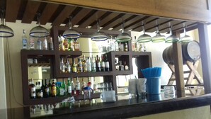 Uma área de bar com estantes de garrafas de bebidas, luminárias pendentes e um barril de madeira.