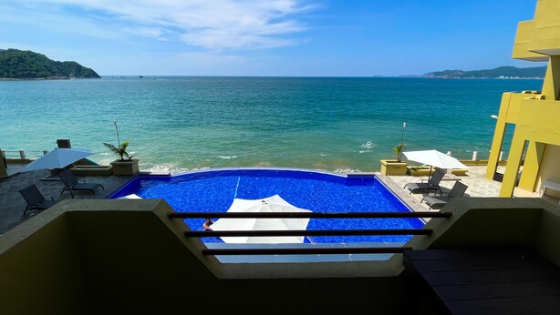 Piscina com vista para o mar, cadeiras de descanso e um edifício amarelo.