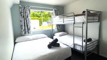 Quarto com beliche, janela, cortinas e vista para o verde lá fora.