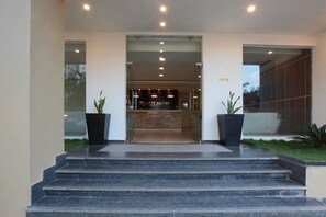 Entrada de um edifício moderno com balcão de recepção, portas de vidro e escada.