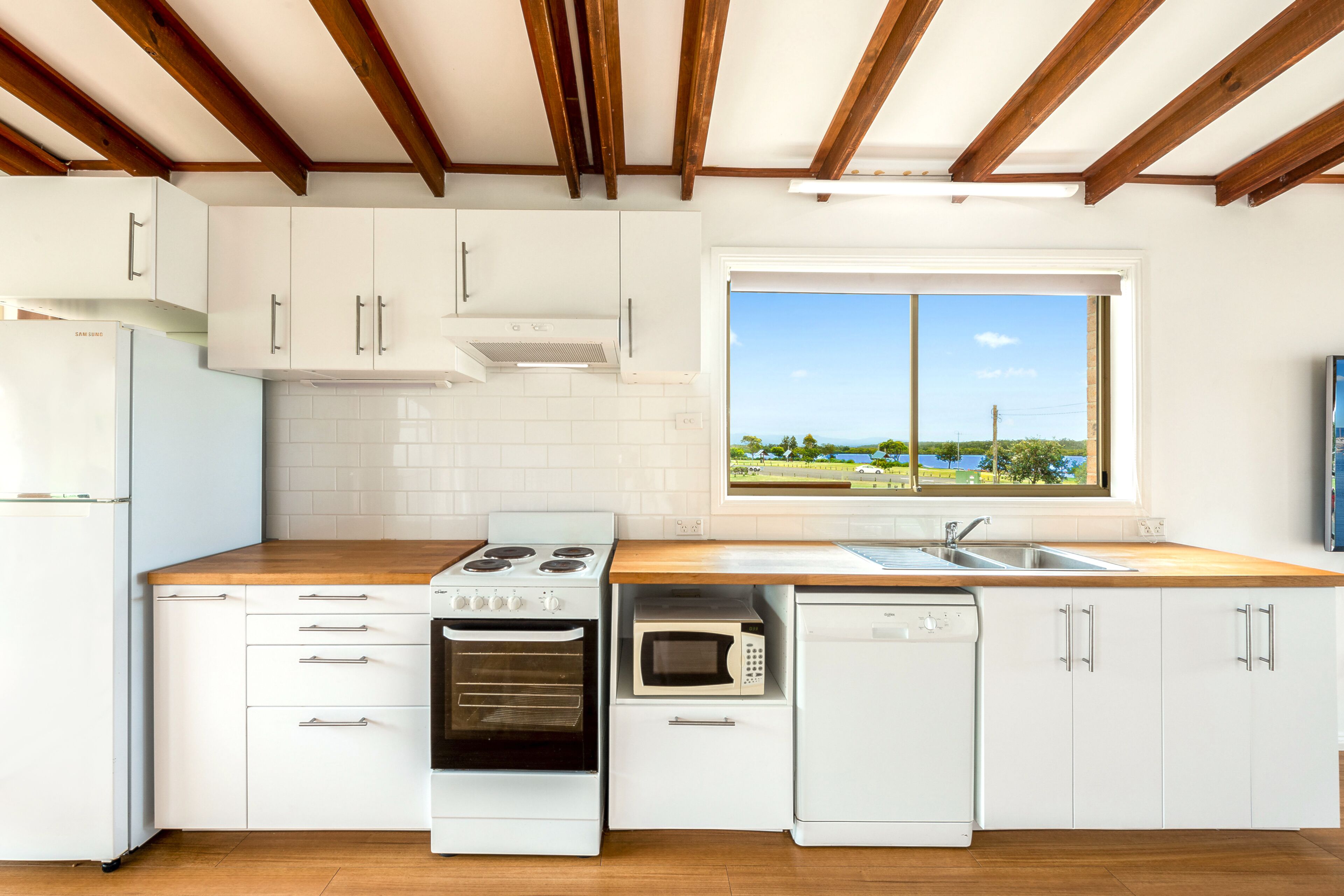 Cozinha moderna com armários brancos, fogão, forno, micro-ondas e janela com vista.