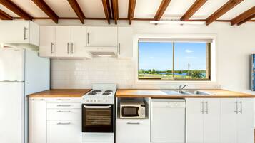 Cozinha moderna com armários brancos, fogão, forno, micro-ondas e janela com vista.