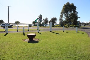 Uma área gramada com um grande jardim elevado, um parquinho infantil com um escorrega e uma estrutura em torre.