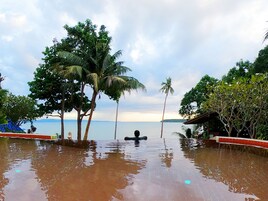 Área externa inundada com palmeiras e vista para o mar.