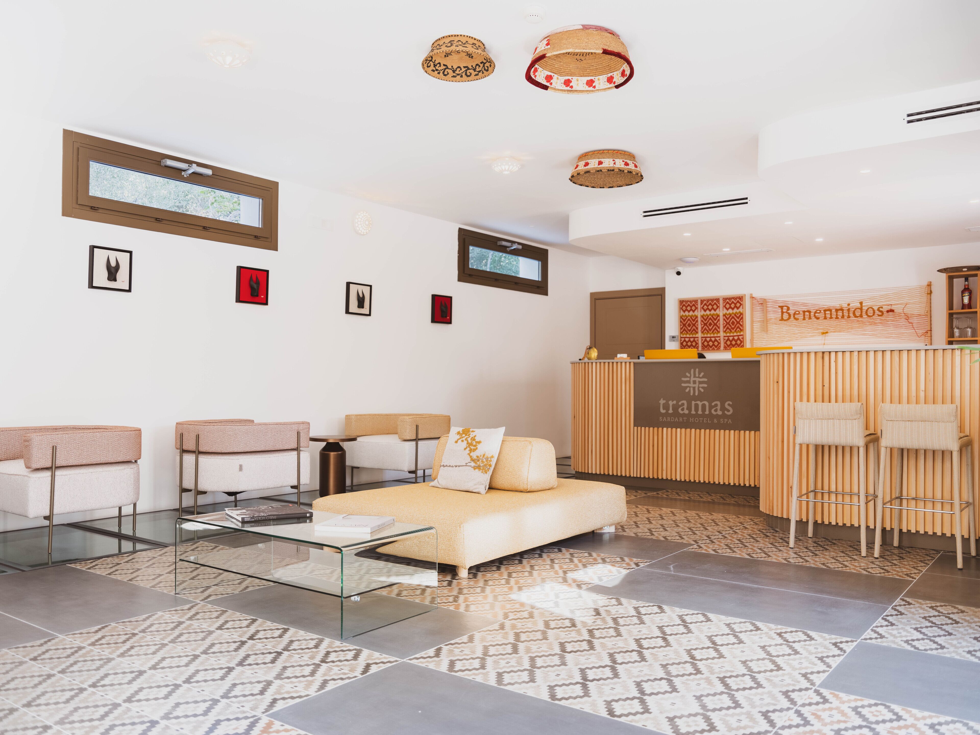 Uma área de recepção de hotel, com balcão de atendimento, duas cadeiras de vime, um sofá e uma mesa de centro de vidro.