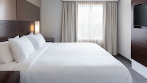 Quarto de hotel com uma cama grande, televisão de tela plana na parede e uma janela com cortinas.