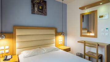 Quarto de hotel com uma cama grande, luminárias de cabeceira, mesa de cabeceira de madeira, escrivaninha com cadeira e espelho fixado na parede.