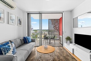 Sala de estar moderna com sofá cinza, mesa redonda de madeira, TV de tela plana e varanda com vista para a cidade.