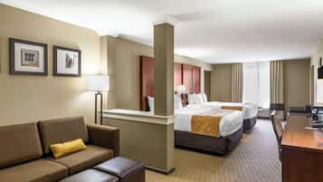 Quarto de hotel com sofá, duas camas, escrivaninha e uma luminária.