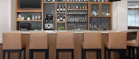 Uma área de bar com várias prateleiras de garrafas, uma máquina de café e uma TV de tela plana.