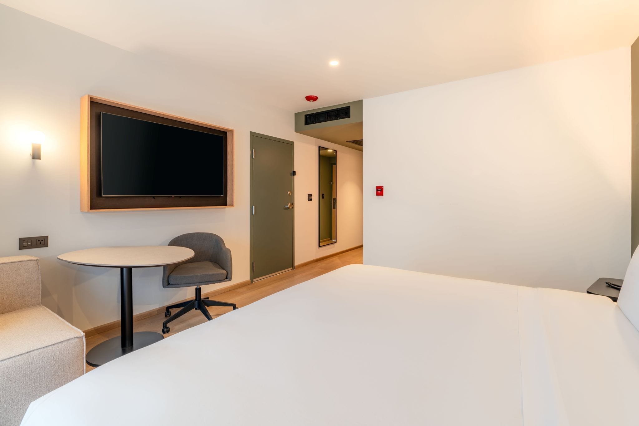 Quarto de hotel com cama, escrivaninha, cadeira, televisão e porta para o banheiro.