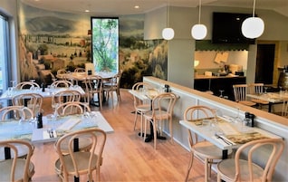 Um restaurante com mesas e cadeiras redondas, um mural na parede e iluminação pendente.