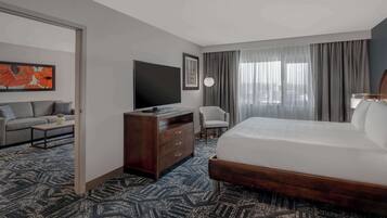 Quarto de hotel com uma cama grande, televisão, escrivaninha, cadeira e sofá.
