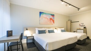 Quarto de hotel com uma cama grande, uma escrivaninha com cadeira, uma mesinha e uma mesa de cabeceira.