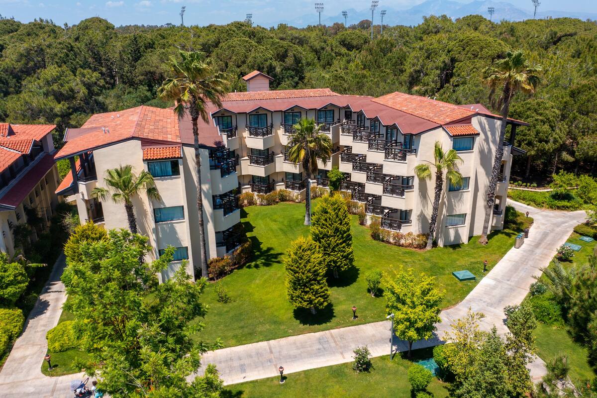 Um hotel de vários andares com telhado de telhas vermelhas, varandas e um gramado bem cuidado com palmeiras.