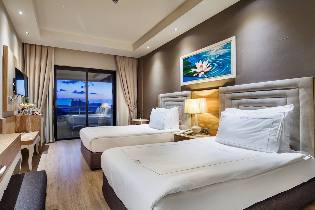 Quarto de hotel com duas camas, televisão, escrivaninha e vista para a cidade.