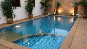 Piscina interna com azulejos azuis, rodeada por plantas em vasos e paredes de pedra.