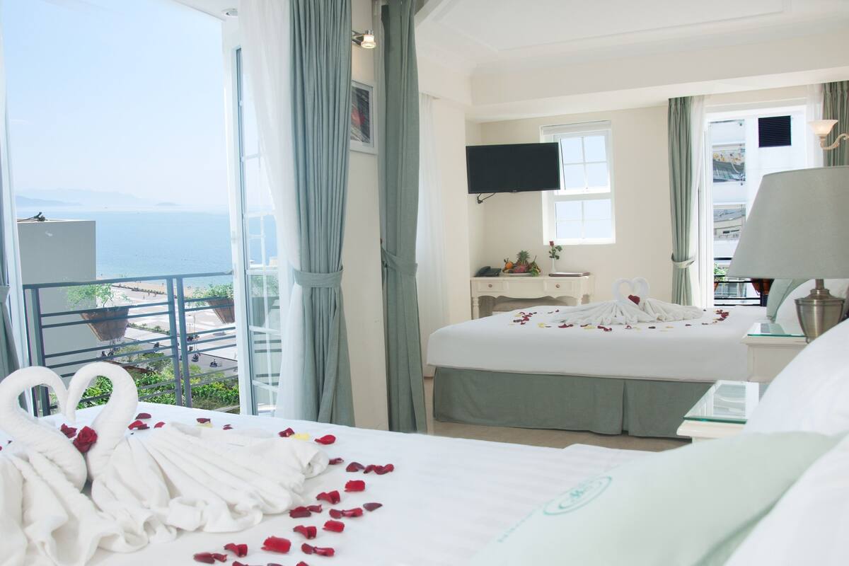 Quarto de hotel com cama, escrivaninha, televisão e varanda com vista para o mar.