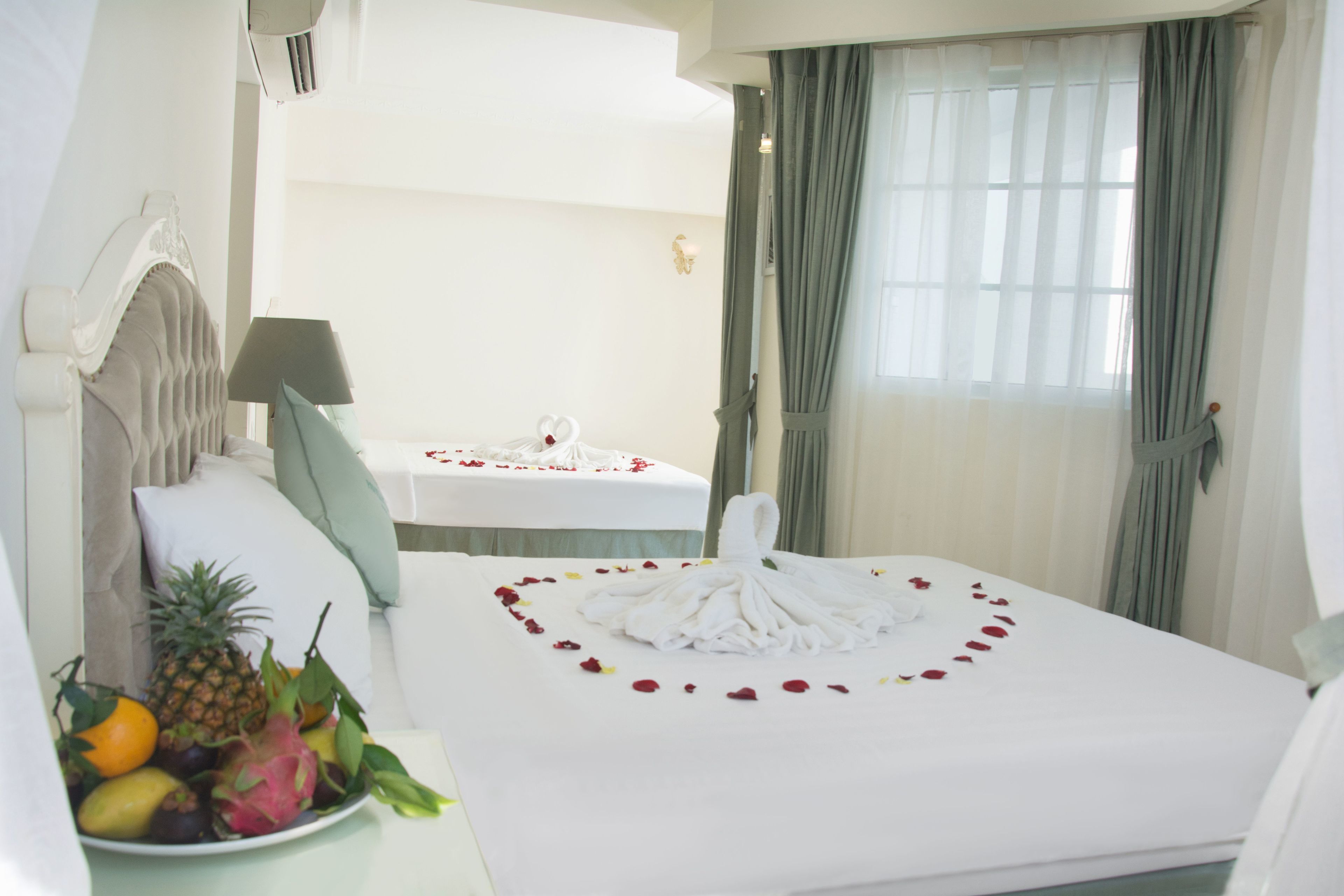 Quarto de hotel com cama bem arrumada, mesa de jantar com toalha branca e uma fruteira ao lado.