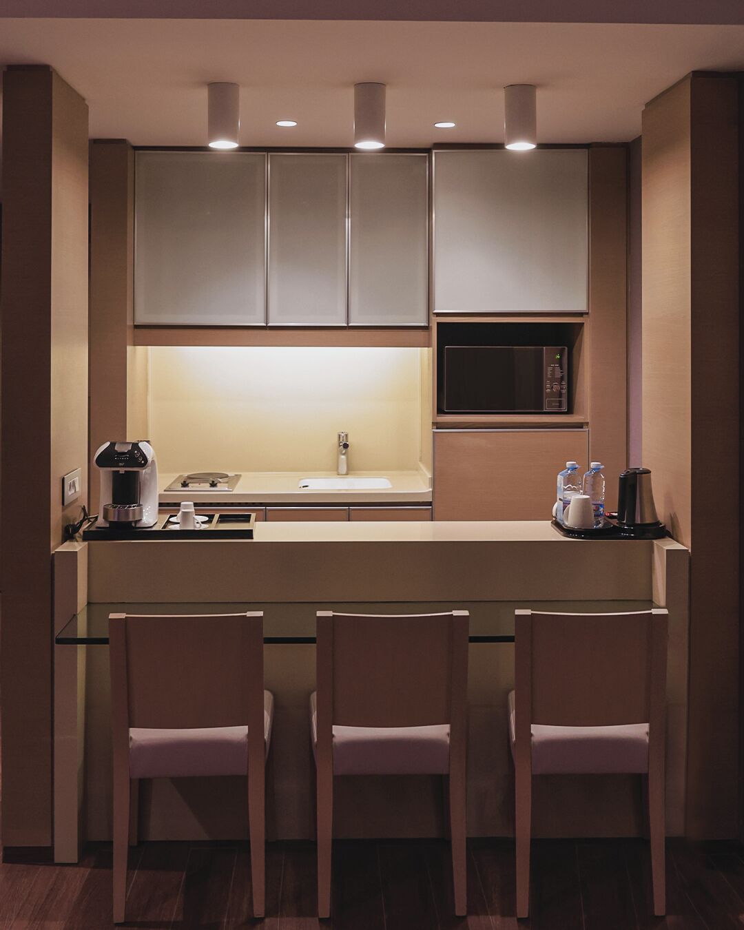 Cozinha compacta com ilha central, micro-ondas e máquina de café. Há três cadeiras em volta da ilha.