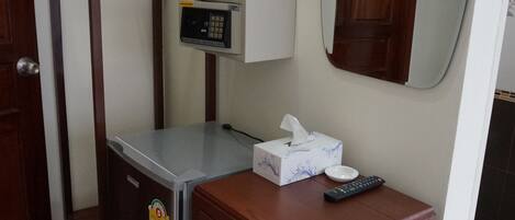 Quarto compacto com armário de madeira, uma mesinha com lenços de papel e controle remoto, micro-ondas e uma lixeira azul.