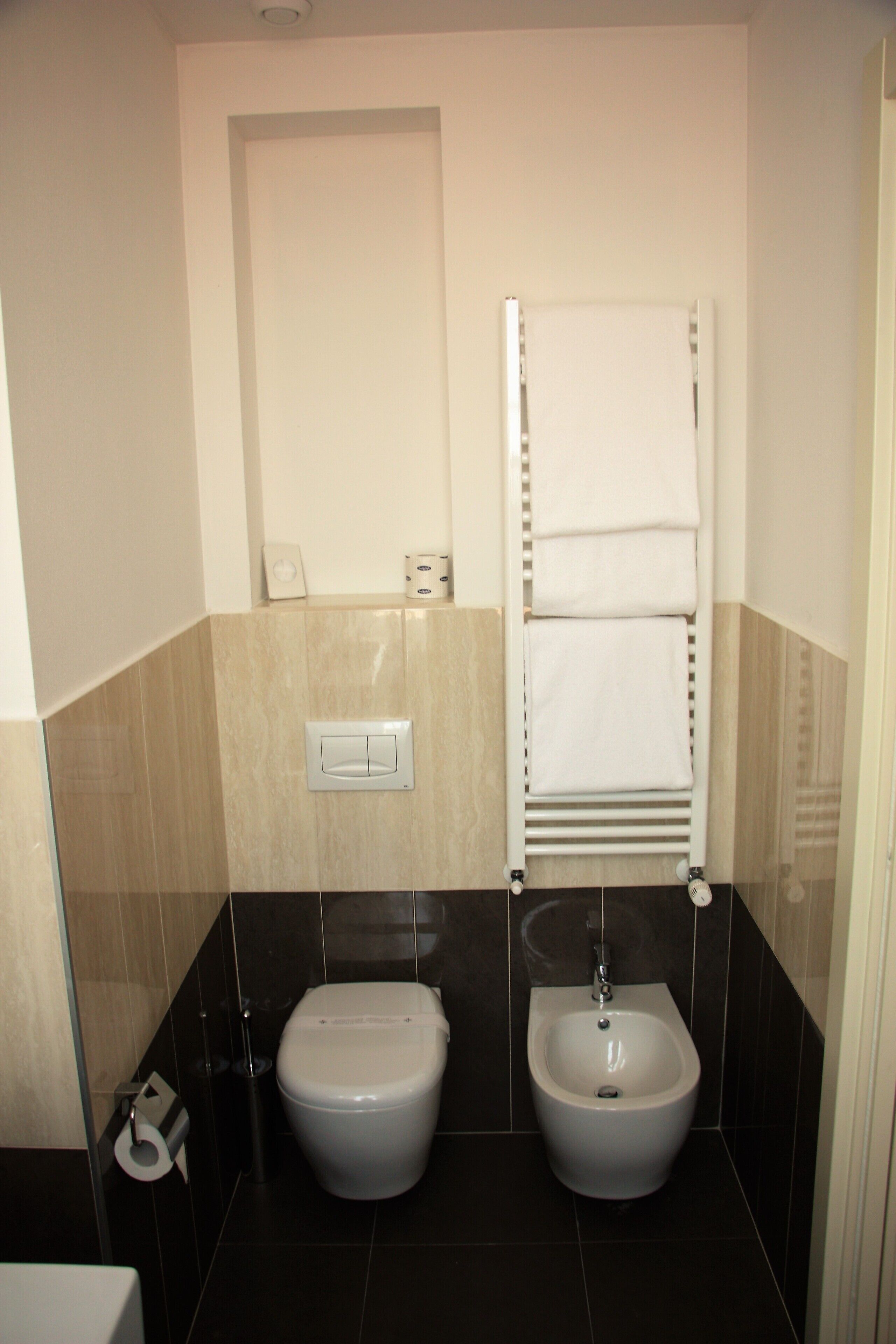 Casa de banho compacta com sanita, bidé e suporte para toalhas.