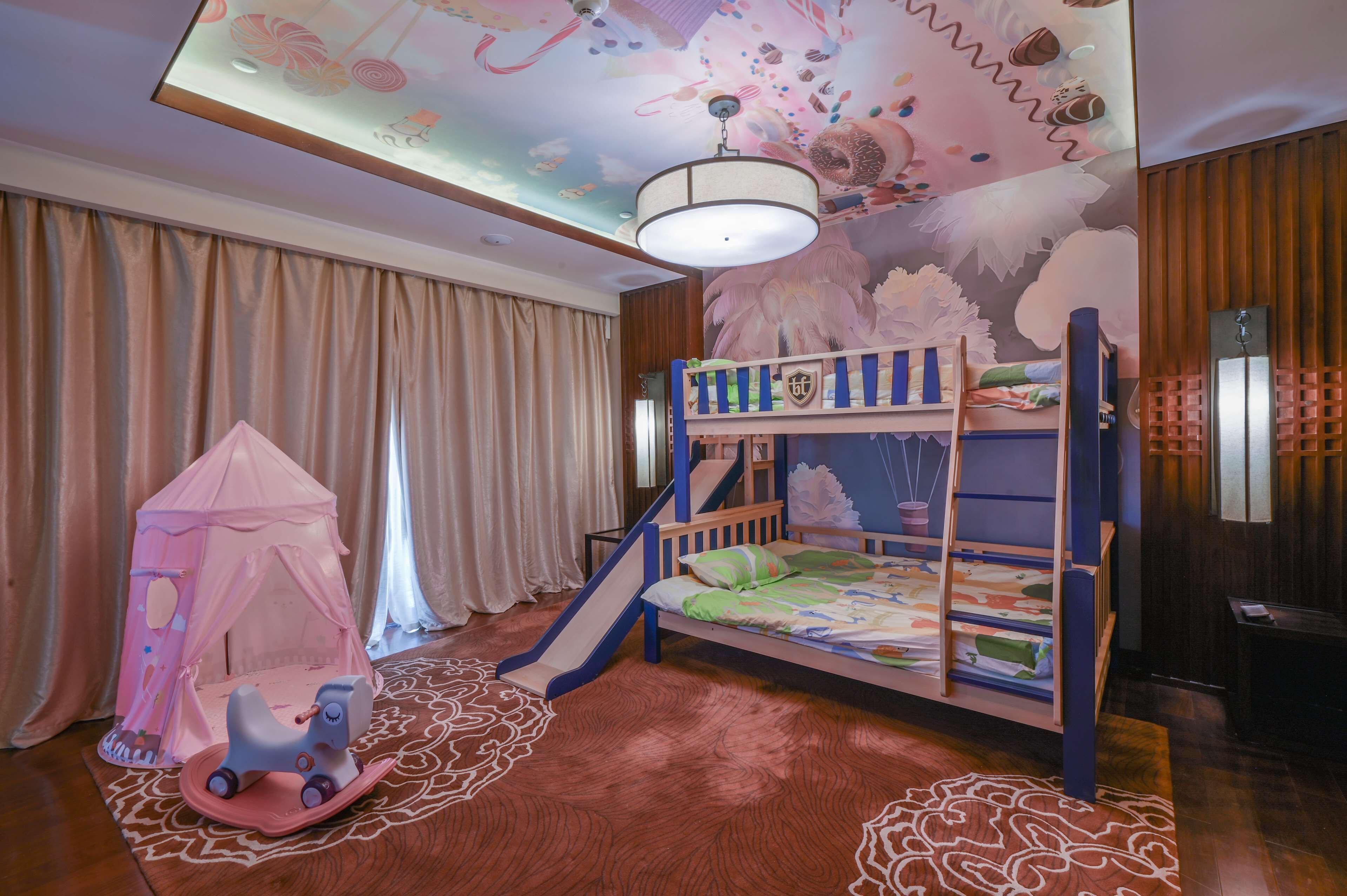 Quarto infantil com beliches, escorrega, tenda e um cavalinho de balanço.