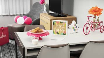 Quarto de hotel com mesa de jantar posta com biscoitos e leite, televisão, vaso com flores e decoração de bicicleta.