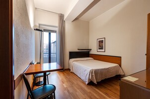 Quarto pequeno e limpo, com uma cama de solteiro, uma escrivaninha e uma cadeira.