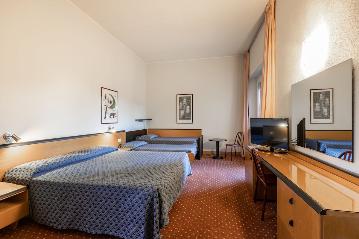 Quarto de hotel com duas camas, uma mesa de escritório com televisão, uma cadeira e uma pequena mesa.