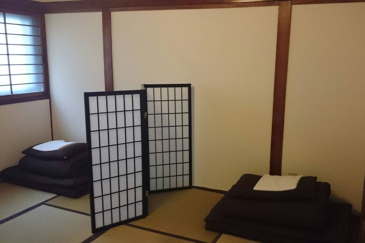 Um quarto japonês tradicional com piso de tatame, um biombô shoji, um sofá de tatame e um pequeno banquinho de tatame.